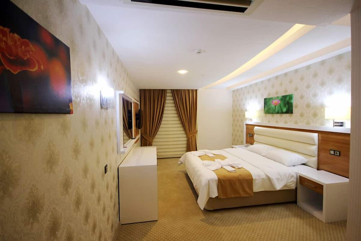 Quarto de hotel com uma cama, mesa de cabeceira, televisão, quadro na parede e escadas ao fundo.