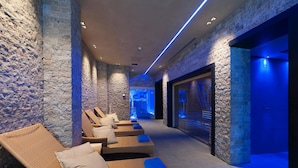 Uma área de spa com paredes de pedra, cadeiras reclináveis e um caminho iluminado em azul.