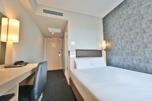Quarto de hotel com cama, escrivaninha com cadeira, espelho e duas luminárias.