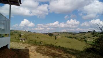 Paisagem rural com colinas ondulantes, céu claro e algumas árvores esparsas.