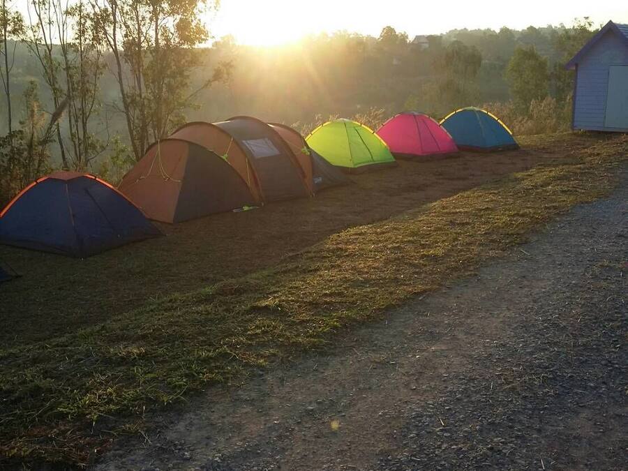 Uma fileira de barracas coloridas numa trilha de terra, com um pequeno galpão ao fundo.