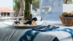 Uma mesa com um menu, um frasco de azeite, um copo de vinho branco e um prato de frutos do mar.