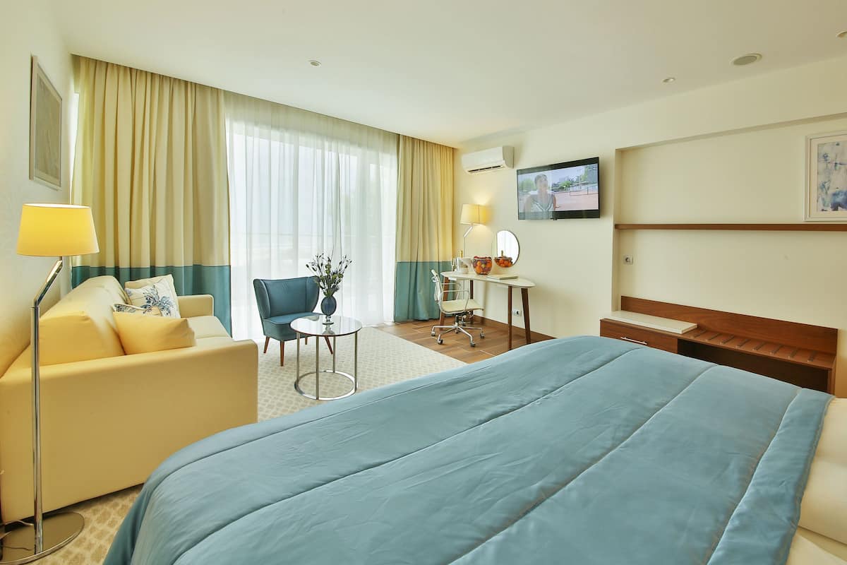 Quarto de hotel com cama, escrivaninha, cadeira, sofá e televisão na parede.