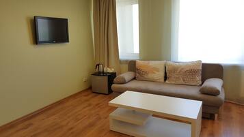 Uma sala de estar com sofá, mesa de centro, TV na parede e janela com cortinas.