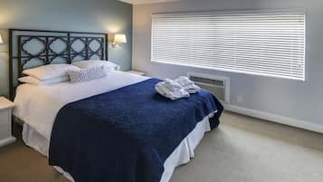 Uma cama bem arrumada com colcha azul e branca, uma cabeceira decorativa e um abajur fixado na parede.