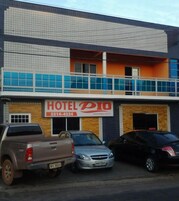 Um edifício de dois andares com uma placa indicando 'HOTEL PIO' e um número de contato. Três carros estão estacionados na frente.