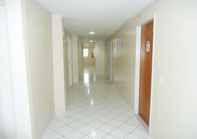 Um corredor comprido e estreito com chão de azulejos brancos e paredes bege.