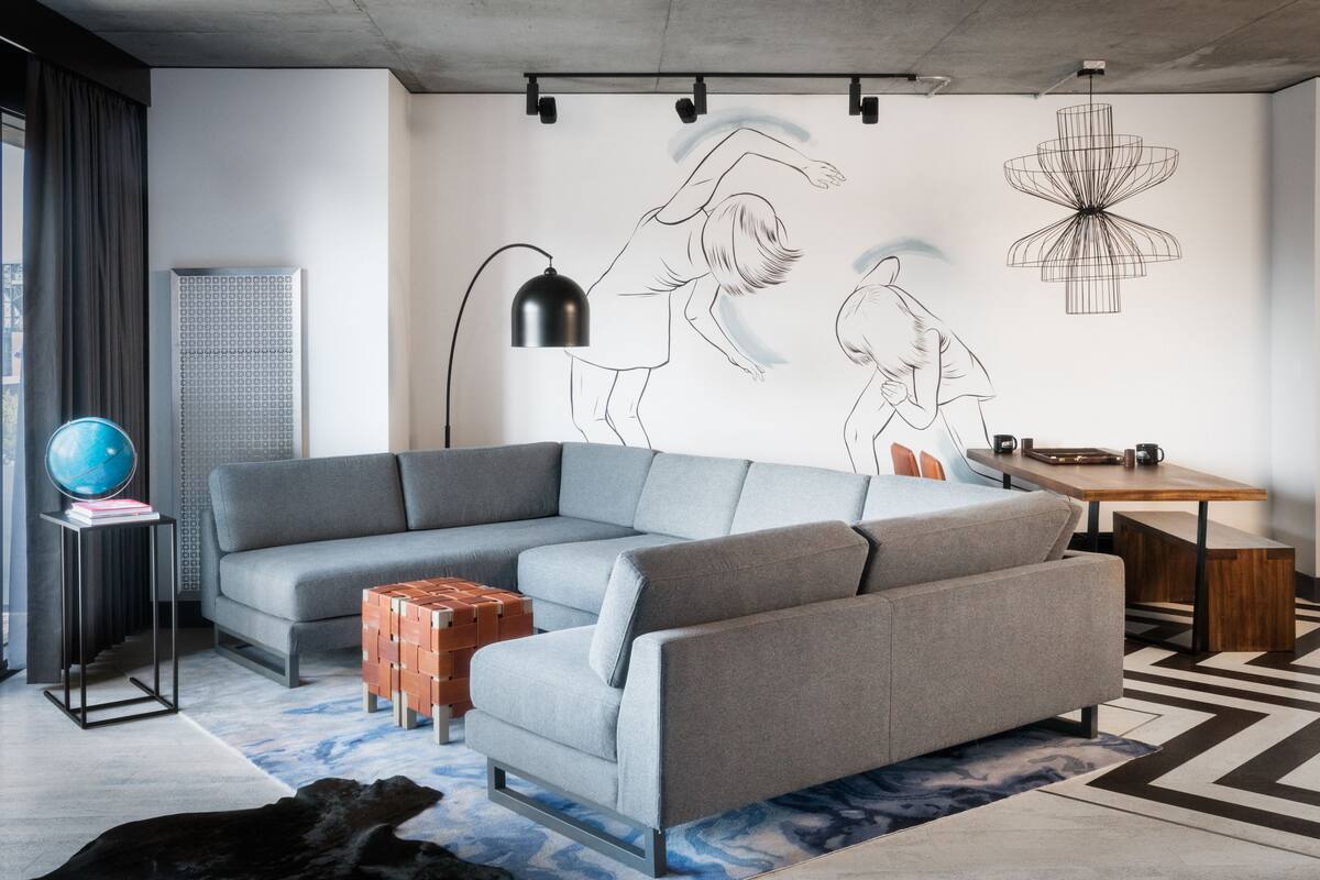 Uma sala de estar moderna com um sofá seccional, um globo em uma mesinha de apoio e uma parede com desenhos abstratos de linhas.