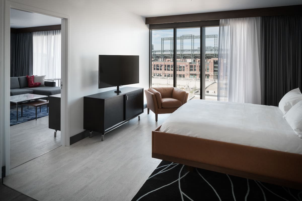 Quarto de hotel moderno com uma cama grande, televisão de tela plana, sofá e vista para a cidade.