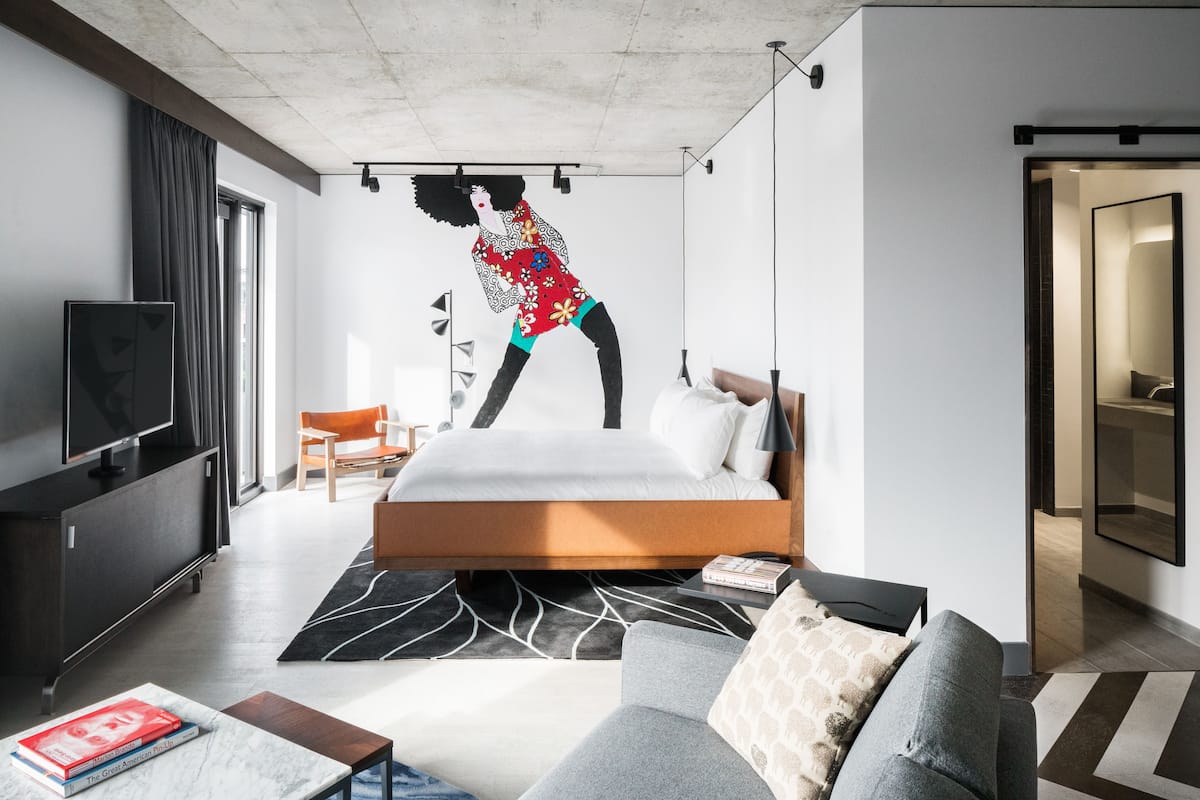 Quarto de hotel moderno com uma cama grande, um sofá, uma TV e uma janela ampla.