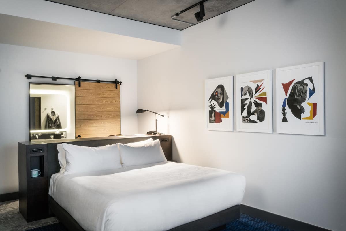 Quarto de hotel com cama, secretária com computador, espelho e três obras de arte emolduradas na parede.