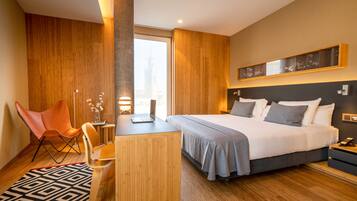Quarto de hotel moderno com uma cama grande, uma escrivaninha com cadeira e vista para um edifício pela janela.
