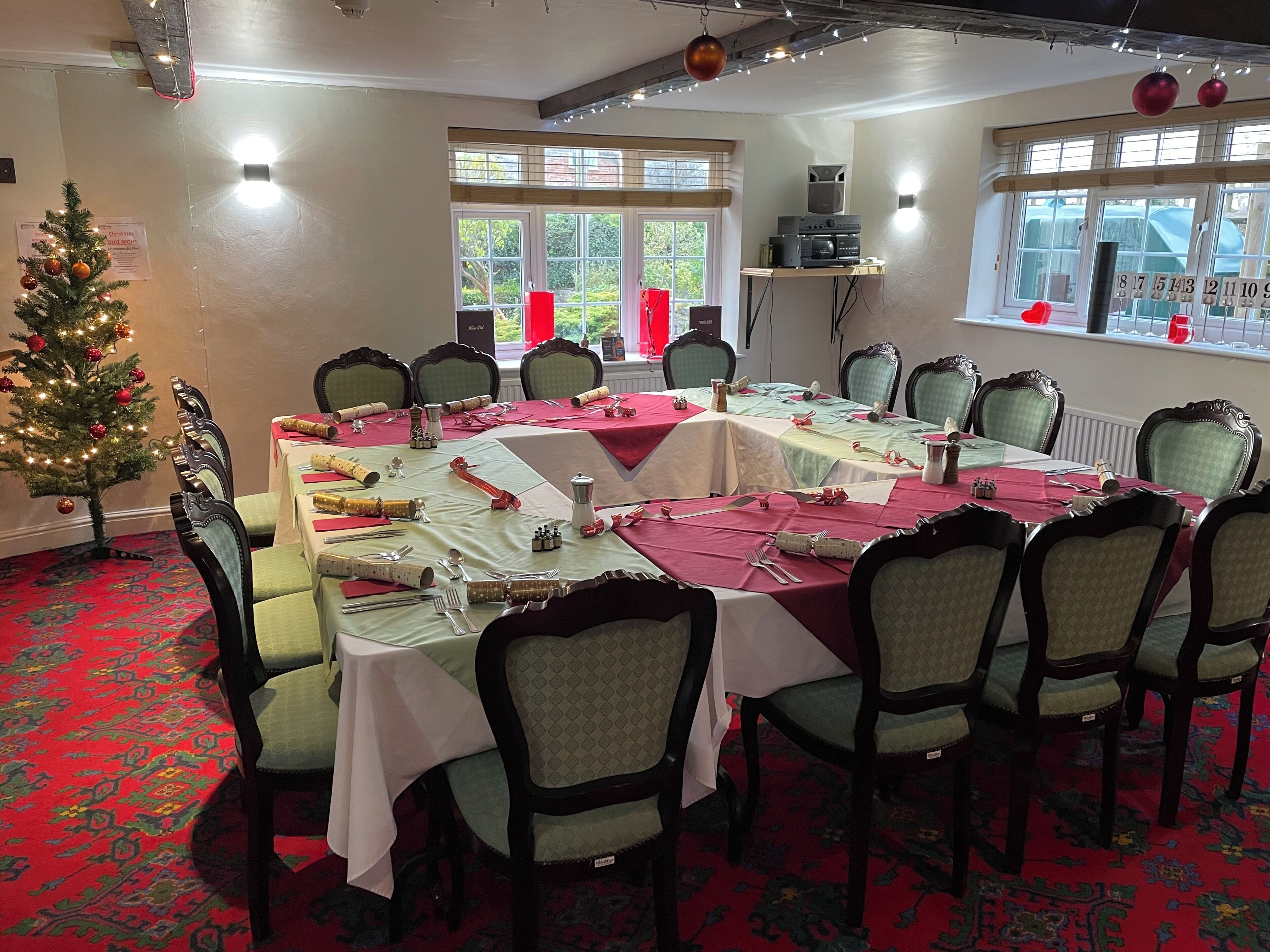 Uma sala de jantar com uma mesa comprida posta para uma refeição, rodeada por cadeiras, um pinheiro de Natal e uma janela com vista.