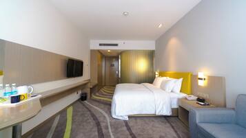 Quarto de hotel com cama, mesa de cabeceira, cadeira, televisão e escrivaninha com espelho e artigos de higiene pessoal.