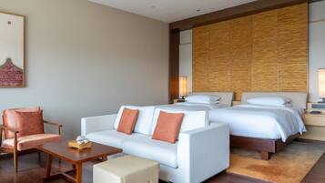 Quarto de hotel com sofá, cadeira, mesa pequena, cama e mesa de cabeceira.
