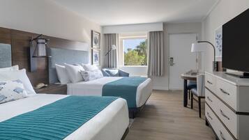 Quarto de hotel com duas camas, uma mesa, uma televisão e uma janela com cortinas.