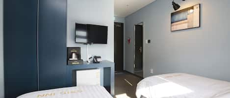 Quarto de hotel com duas camas, uma escrivaninha com televisão de tela plana, cafeteira e um quadro na parede.