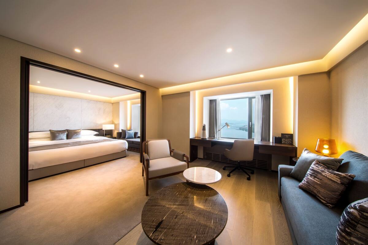 Quarto de hotel moderno com cama, escrivaninha, sofá e mesa de centro.