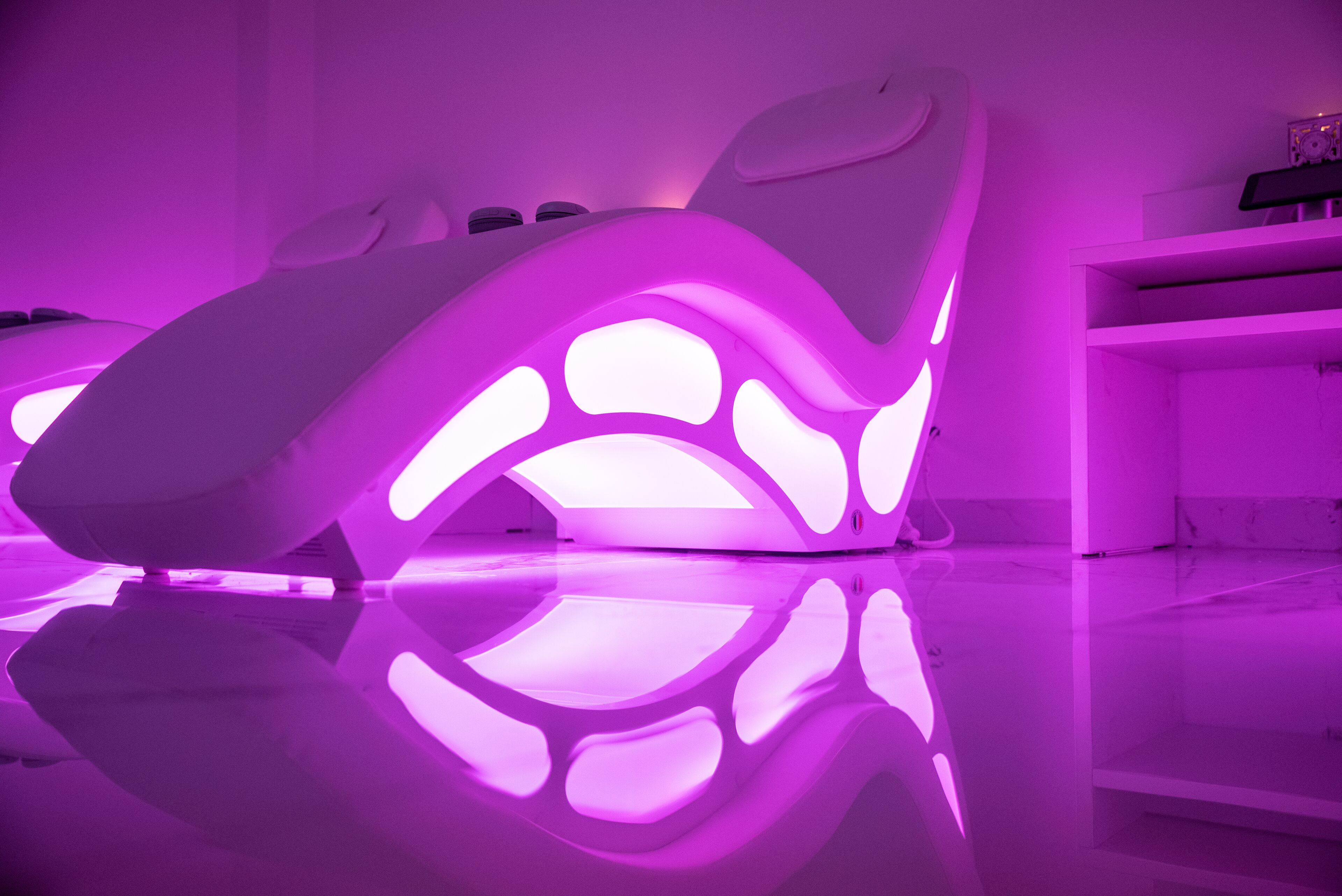 Uma cadeira moderna e de design único em formato de sapato, com superfície refletora, diante de um fundo iluminado em roxo.
