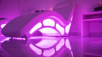 Uma cadeira moderna e de design único em formato de sapato, com superfície refletora, diante de um fundo iluminado em roxo.