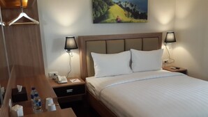 Quarto de hotel com uma cama, duas mesas de cabeceira, uma escrivaninha de madeira, um cabideiro e um quadro na parede.