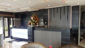 Uma área de recepção moderna com divisória de vidro, balcão de atendimento e espaço de estar com duas cadeiras e uma mesa.