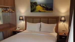 Quarto de hotel com uma cama grande, duas mesas de cabeceira, um telefone, um controle remoto e um quadro na parede.