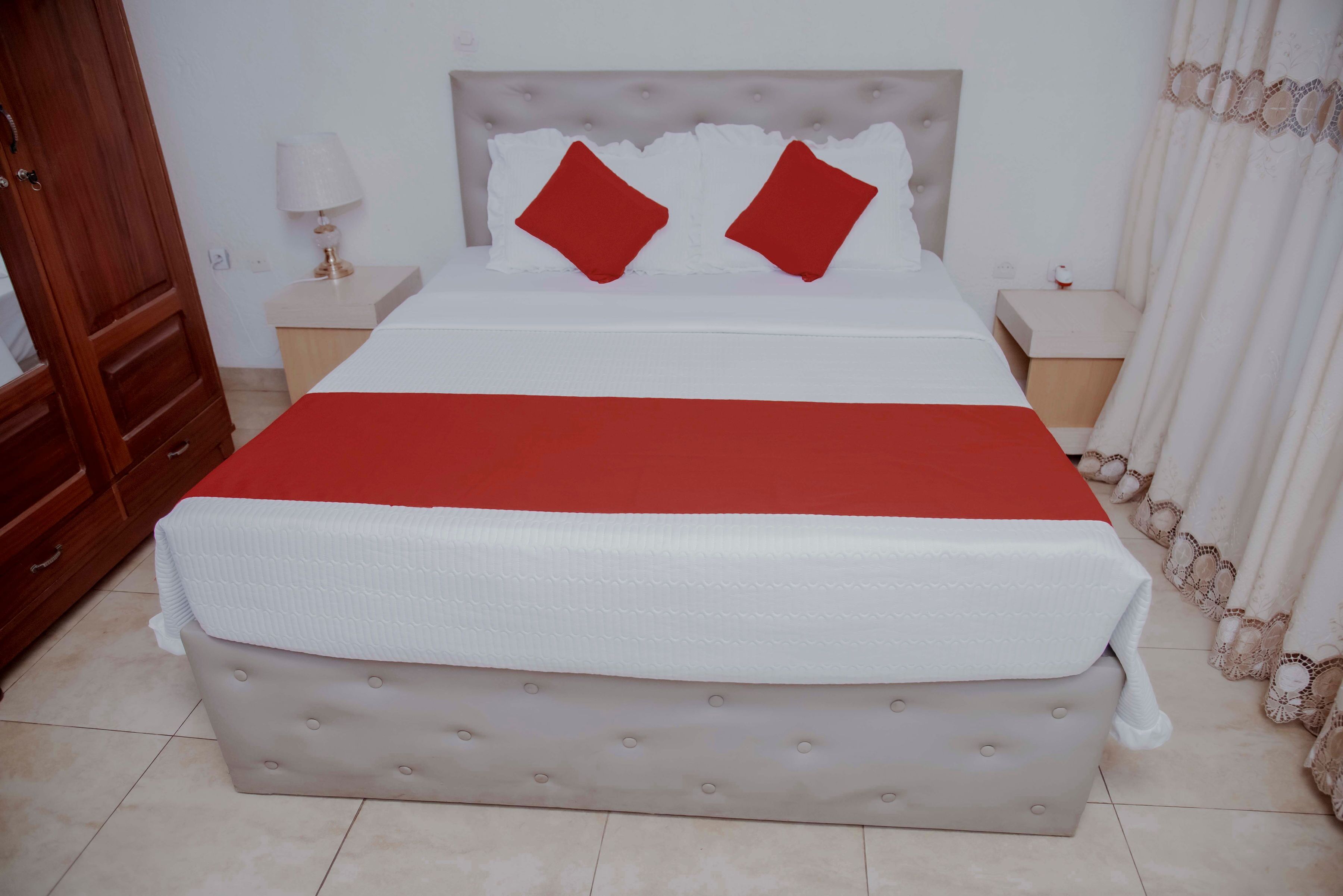 Uma cama bem arrumada com um cobertor vermelho, duas almofadas vermelhas e uma cabeceira estofada.