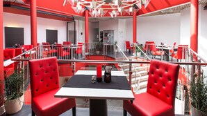 Um restaurante moderno com cadeiras e mesas vermelhas, teto de vidro e um lustre central.