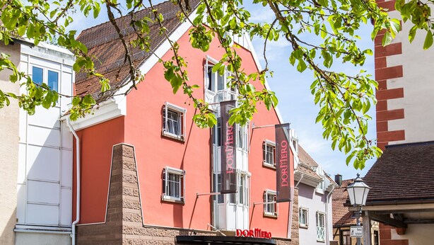 Um edifício vermelho com uma placa que diz "DORMIER" e uma placa para o "franziskaner museum" ao fundo.