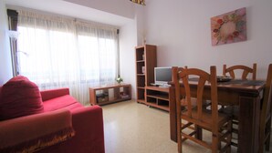 Uma sala de estar com um sofá vermelho, uma mesa de jantar de madeira com cadeiras, uma televisão em um móvel e uma estante de livros.