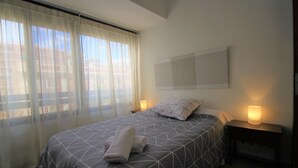 Uma cama bem arrumada com um edredom estampado em padrão geométrico e uma toalha enrolada sobre ela. Existem duas luminárias de cabeceira de cada lado da cama.