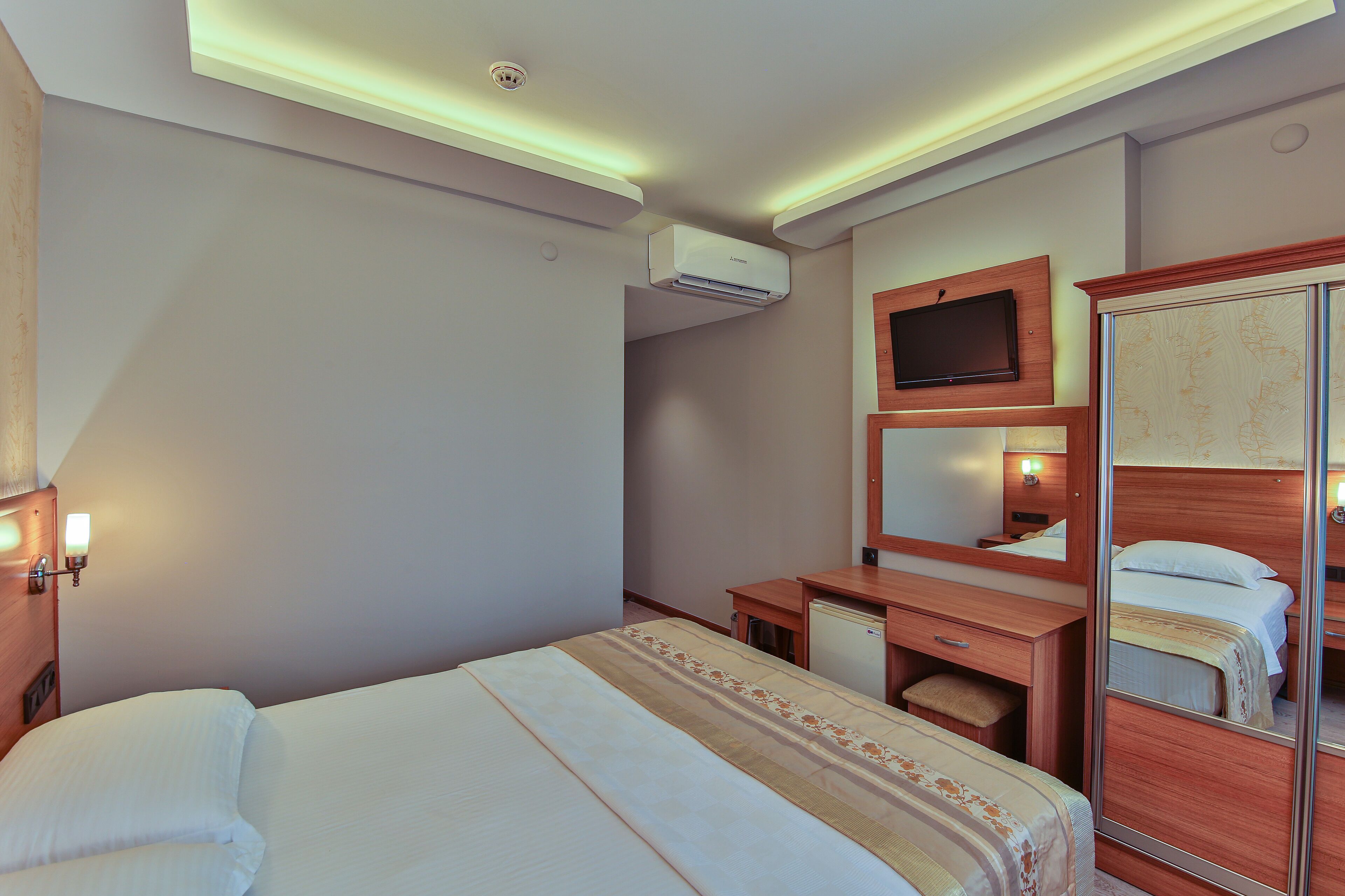 Quarto de hotel com uma cama, uma escrivaninha, um espelho e um ar condicionado.