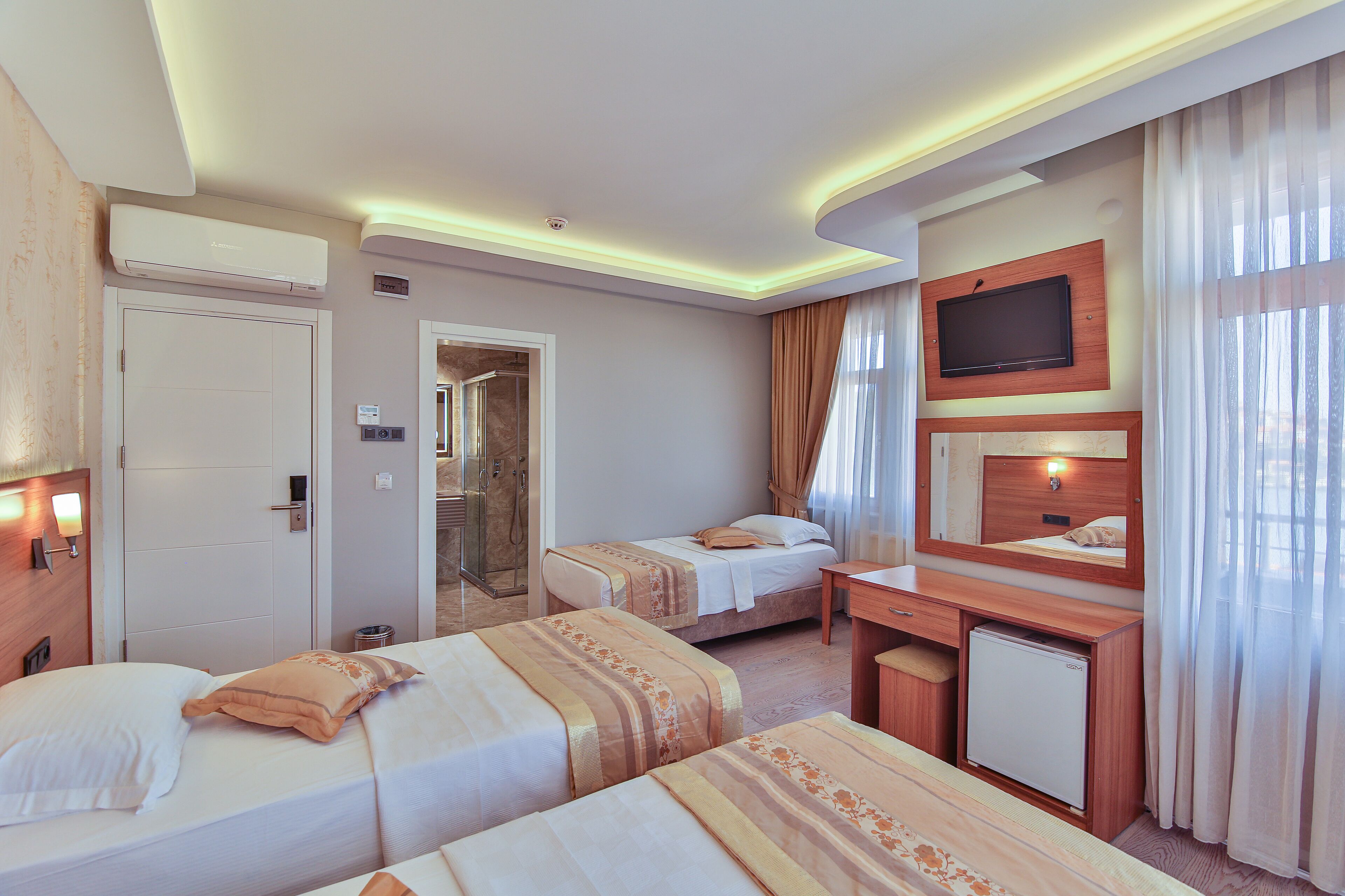 Quarto de hotel com duas camas, uma escrivaninha, televisão e ar condicionado.