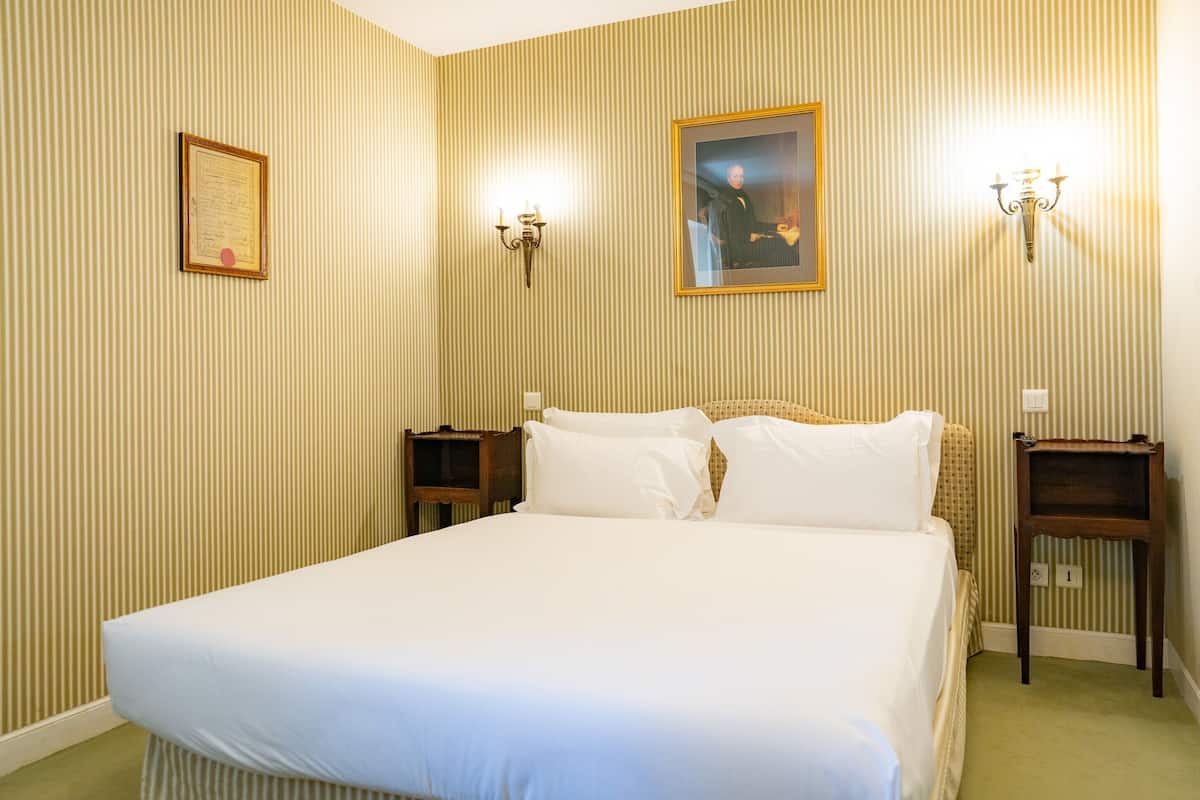 Quarto de hotel com uma cama grande, duas mesas de cabeceira, um certificado emoldurado na parede e um quadro sobre a cama.