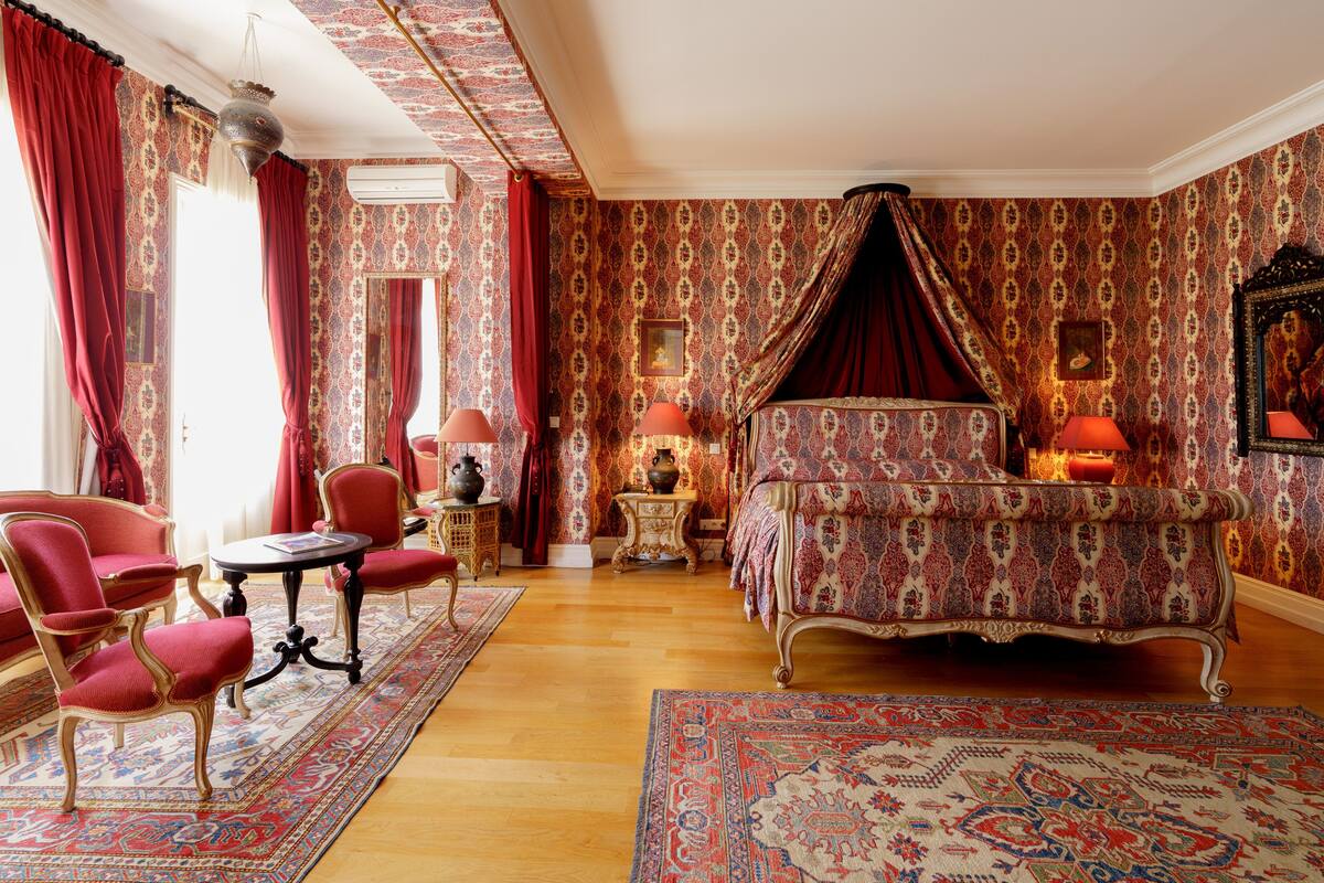 Um quarto com uma cama, duas cadeiras, uma mesa e um tapete.