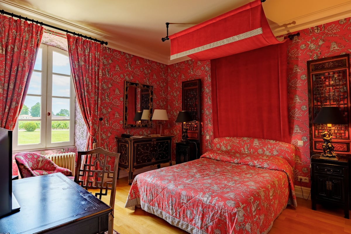Quarto com cama grande, escrivaninha, cadeira e janela com cortinas.
