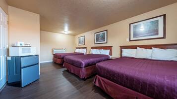Quarto de hotel com três camas, um frigorífico e um quadro na parede.
