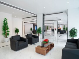 Um lobby moderno com sofás de couro preto, uma mesa de centro de vidro e plantas em vasos.
