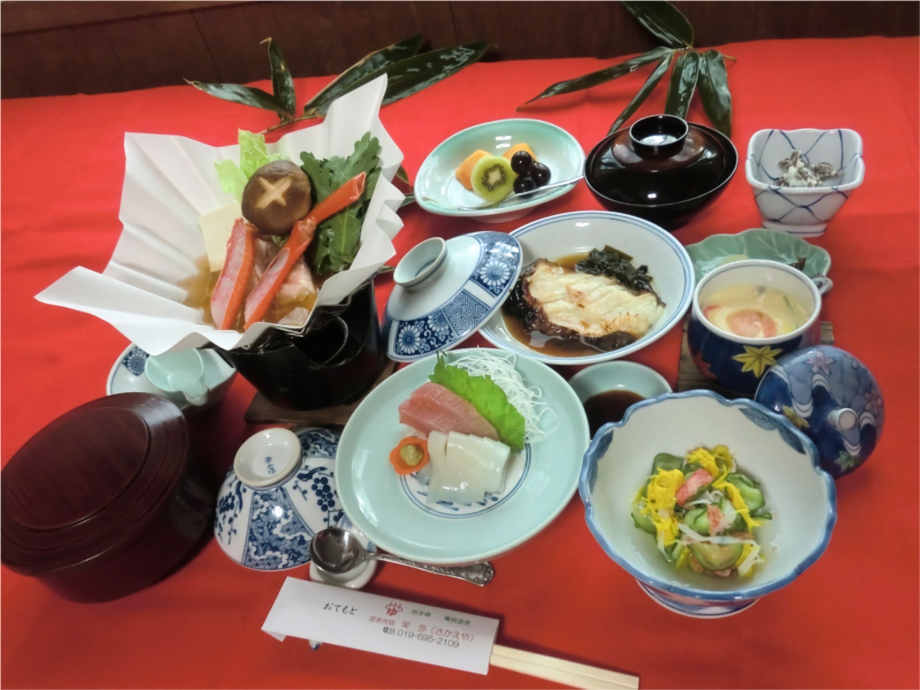 Uma refeição tradicional japonesa com diversos pratos e utensílios sobre uma toalha vermelha.