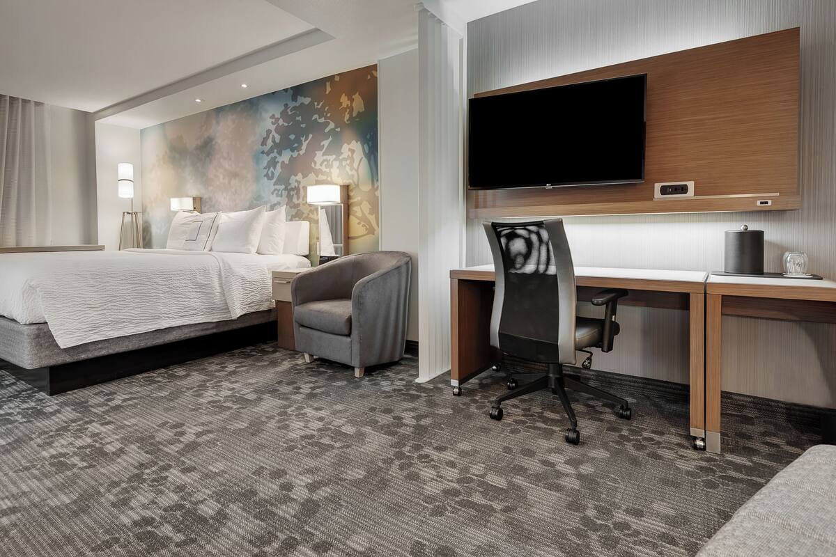 Quarto de hotel com cama, escrivaninha, cadeira, televisão de tela plana e abajur.