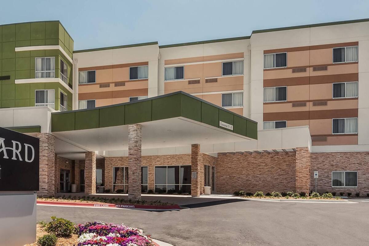 Entrada de um hotel Courtyard Marriott com design moderno, destacando uma placa, uma área de estacionamento coberta e fachada de tijolos.