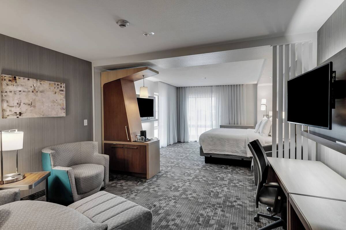 Quarto de hotel moderno com uma cama grande, uma escrivaninha, uma cadeira, uma TV e um quadro na parede.