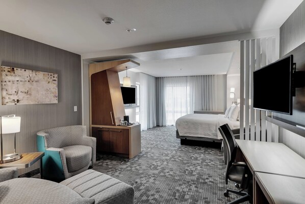 Quarto de hotel moderno com uma cama grande, uma escrivaninha, uma cadeira, uma TV e um quadro na parede.