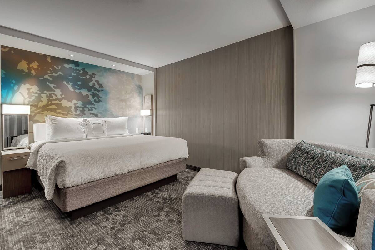 Quarto de hotel moderno com uma cama grande, um sofá, uma mesinha e uma parede com padrão de camuflagem.
