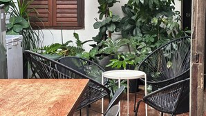 Área externa com mesas e cadeiras, rodeada por diversos vasos de plantas.
