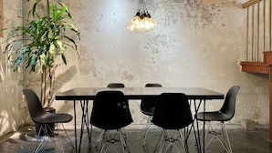 Uma sala de conferências com uma mesa grande, quatro cadeiras, um lustre e um vaso de planta.