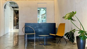 Um espaço amplo e interno, com piso de concreto, ventilador de teto e duas cadeiras próximas a uma pequena mesa.