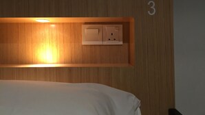 Quarto de hotel com cabeceira de madeira, uma tomada elétrica na parede e o número '3' indicando o número do quarto.