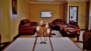 Uma sala de estar com televisão, sofás de couro, uma mesa de jantar e um vaso com velas.